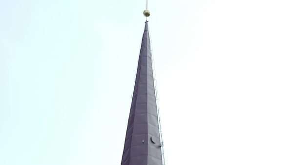 Tilt shot of Catholic church with high cone roof and big green trees ...