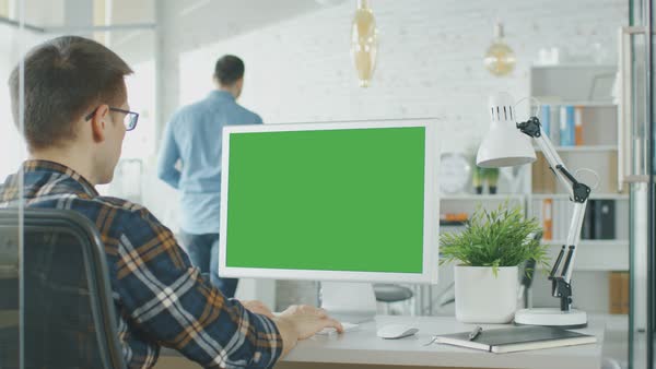 Close-up of a man sitting at his desk with green screen pc on the table ...