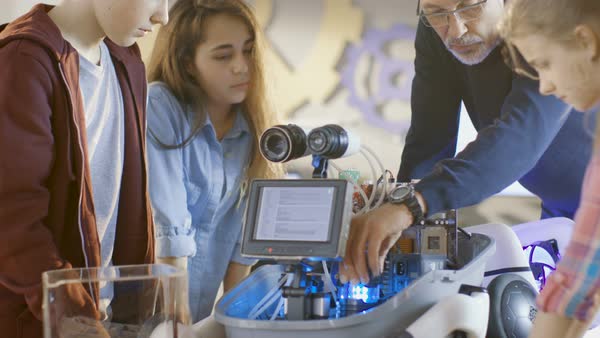 Teacher and his pupils work on a programable robot with led ...