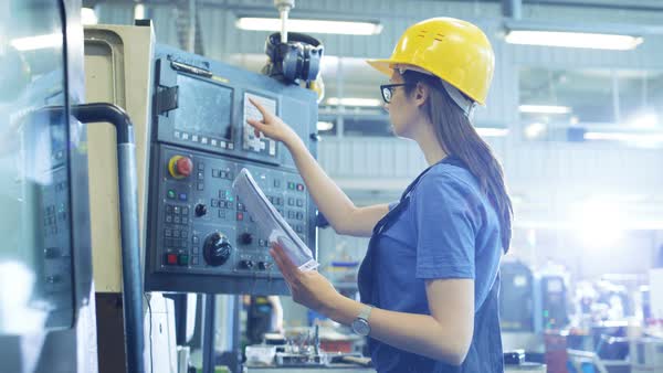 Professional female operator in hard hat setting up/ programming CNC ...