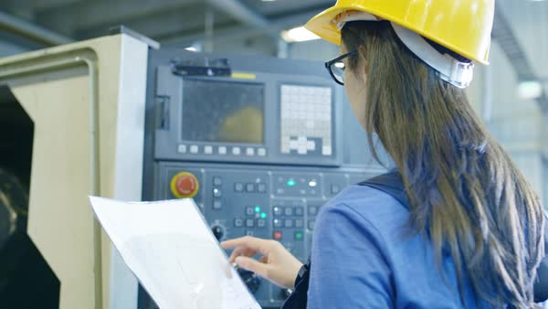 Professional female operator in hard hat setting up/ programming CNC ...