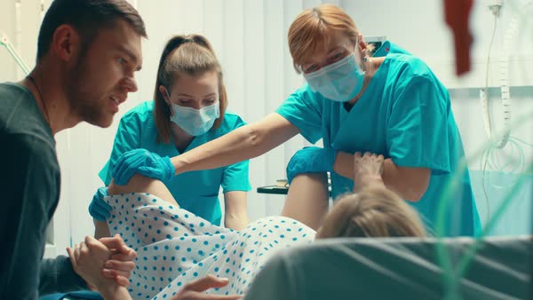 In the hospital woman giving birth, husband holds her hand in support ...