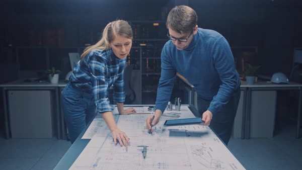 Male and female engineers talk and work on blueprints using conference ...