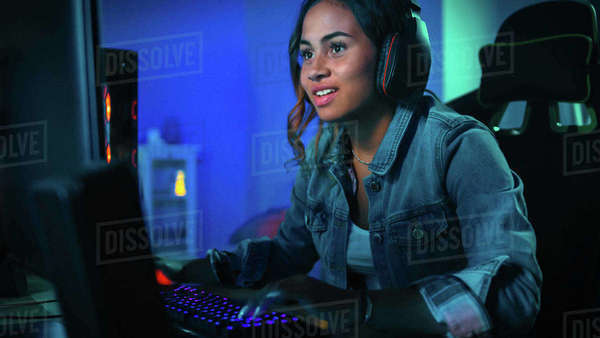 Pretty and excited black gamer girl in headphones is playing first ...
