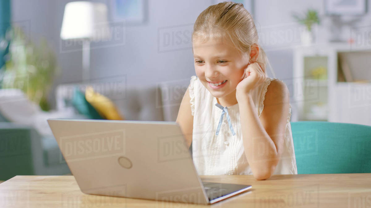 Cute Little Girl Uses Laptop While Sitting at the Desk in the Living ...