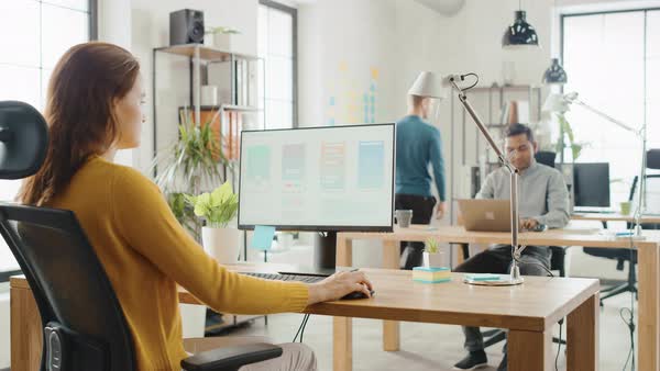 Female mobile software developer sitting at her desk using desktop ...