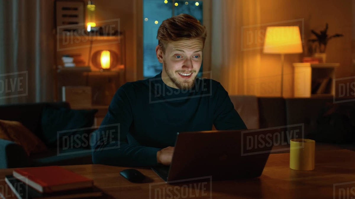 Handsome Smiling Man Works on a Laptop while Sitting at His Desk at ...