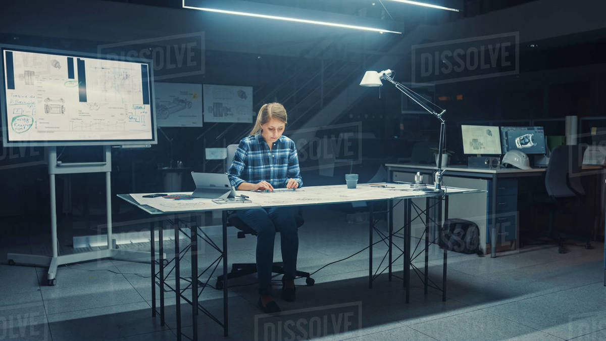 Female Engineer Sitting at Her Desk Works with Blueprints Laying on a ...