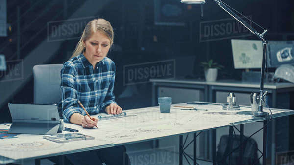 Female Engineer Sitting at Her Desk Works with Blueprints Laying on a ...