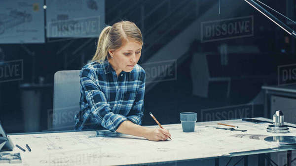 Female Engineer Sitting at Her Desk Works with Blueprints Laying on a ...