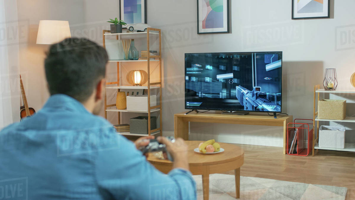 In the Living Room Man Sitting on a Couch Holds Controller Playing in a ...