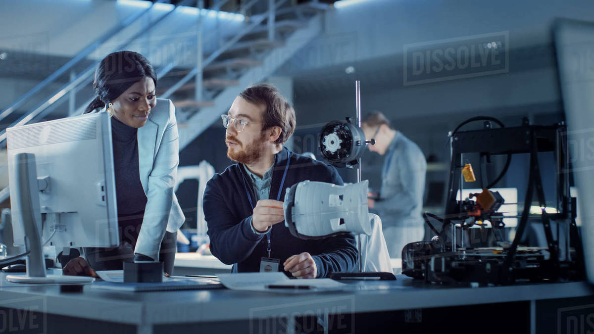 Electronics Development Engineer Working at His Desk, Talks with ...