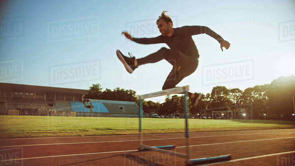 Shot of Athletic Fit Man in Grey Shirt and Shorts Hurdling and Jumping ...