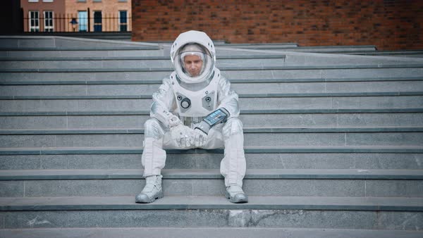 Sad Man in Spacesuit is Sitting on Concrete Stairs. Astronaut is ...