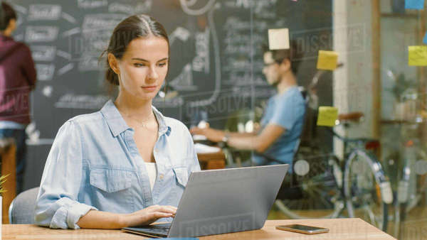Young Female Creative Designer Works on a Laptop. I the Background Team ...