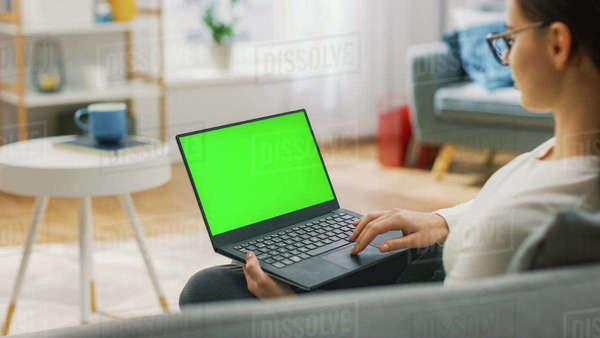 Young Woman at Home Sitting on a Couch Works on a Laptop Computer with ...