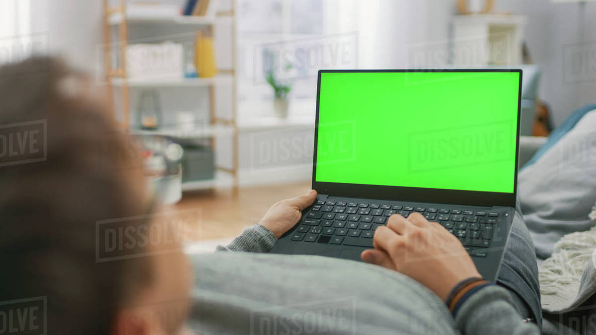 Man at Home Laying on a Couch Using with Green Mock-up Screen Laptop ...