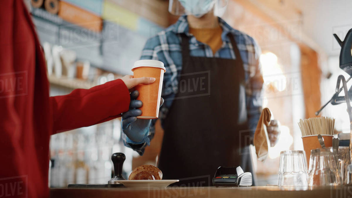 Close-up view of a barista in a face shield handing a cup to a customer ...