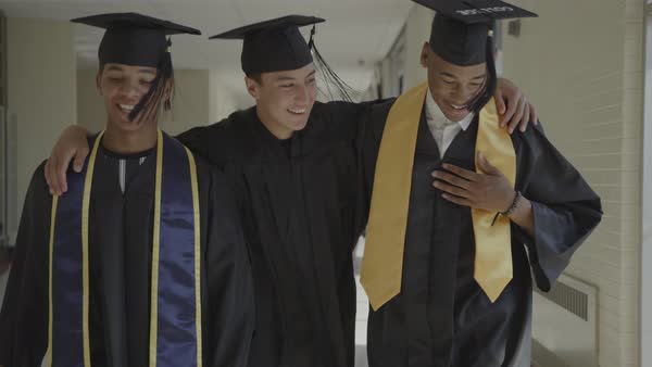 Tracking shot of teenage boys graduating from high school celebrating ...