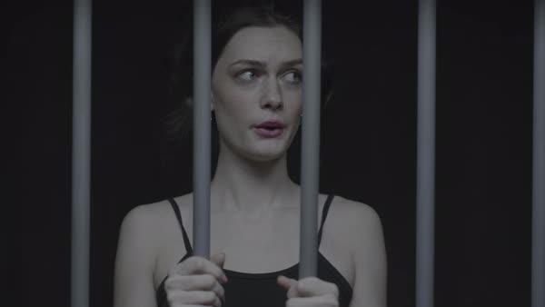 Tilt up to crying woman standing behind bars in prison cell / Cedar ...