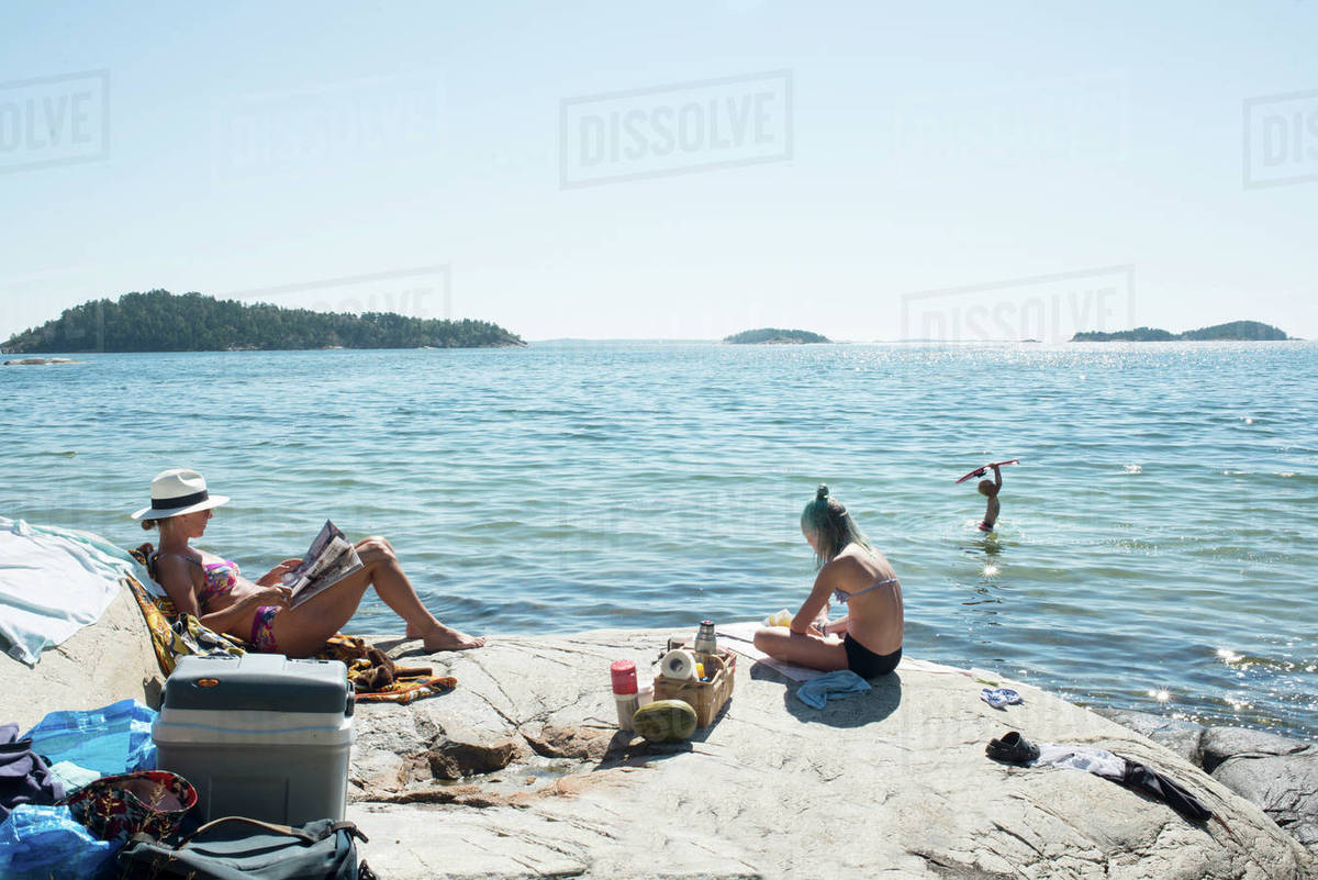 Mother sunbathing and children playing by sea - Stock Photo - Dissolve