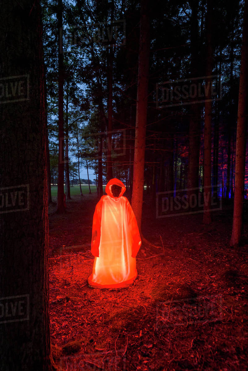 Illuminated human figure in red robe in forest - Stock Photo - Dissolve