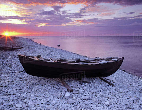 Rowboat on rocky beach at sunset - Stock Photo - Dissolve