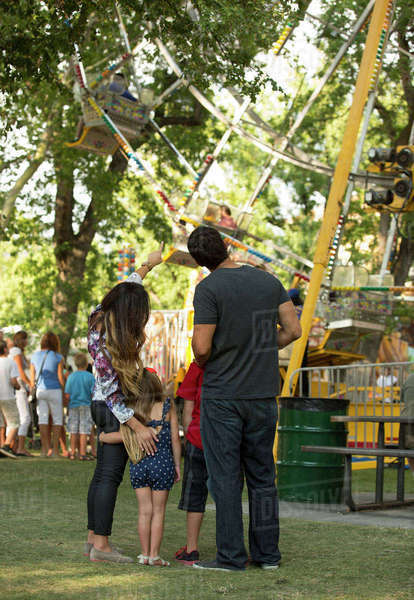 Family admiring spinning ferris wheel ride at amusement park fun fair ...