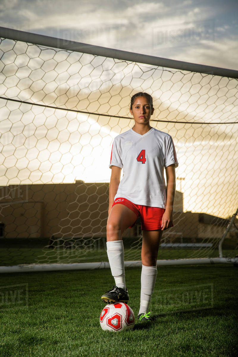 Portrait of soccer player standing with ball in goal under sunset sky ...