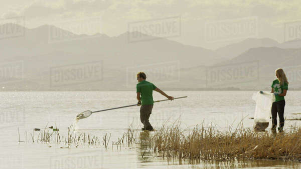 Volunteers collecting recycling and trash garbage on remote grassy lake ...