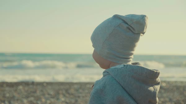 Little cute boy on an empty beach looking at the amazing sea with foam ...