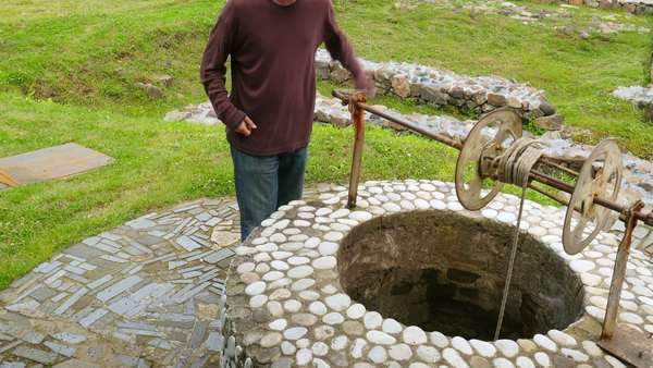 Man taking water from historical fountain well, rope barrel container ...