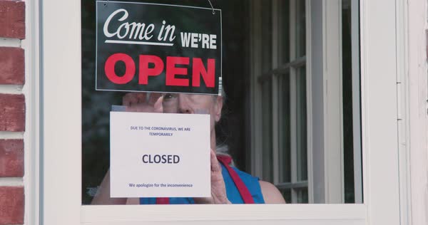 A worried mature small business owner turns the sign on her storefront ...