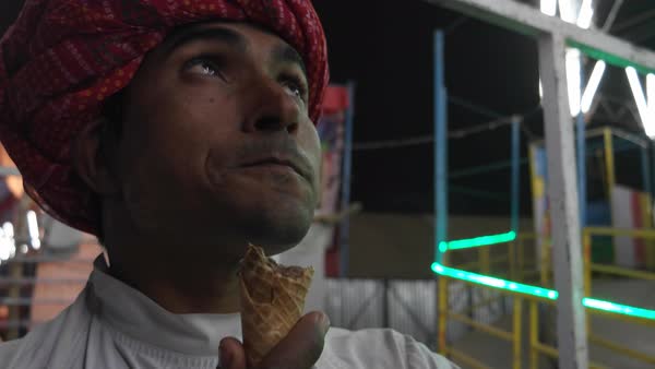 Indian man eating ice cream and looking at the Pushkar Mela carnival ...