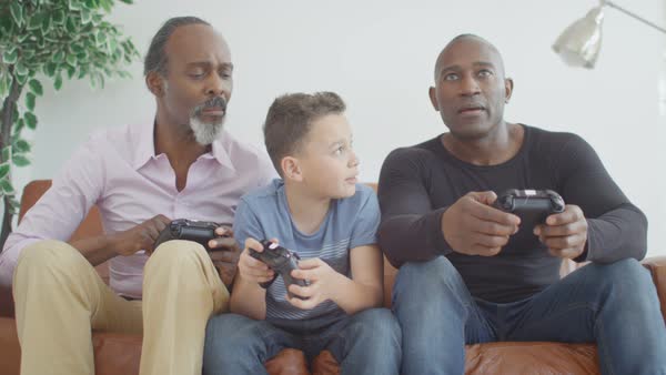 3 Male generations of happy family playing video games together at home ...