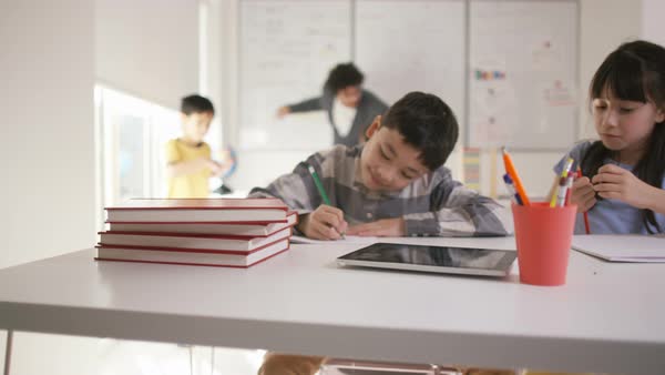 Portrait of happy little boy working at his desk in school classroom ...