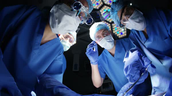 Surgeons working on patient in operating room, seen from patient pov ...