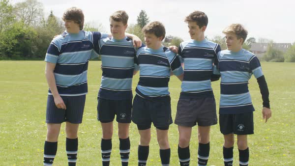 Portrait of smiling teen group standing together on school sports field ...