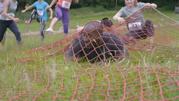Competitors in obstacle course race running and crawling under net on ...