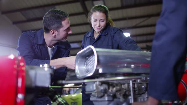 Team of male and female mechanics working on a car engine in garage ...