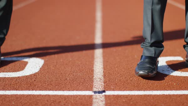 Unrecognisable businessmen at running track line up at starting line ...