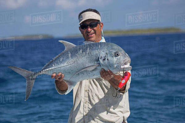 Fisherman holding a giant trevally fish (Caranx ignobilis); Tahiti ...