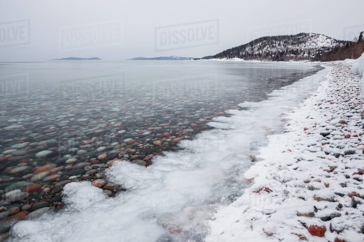 Pebbles in calm water with ice and snow along the shoreline of Lake ...