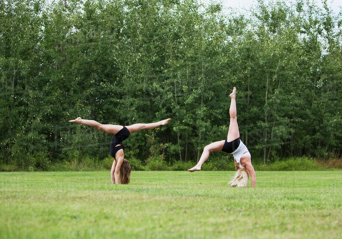 Two teenage gymnasts practicing their routines outdoors in a park ...
