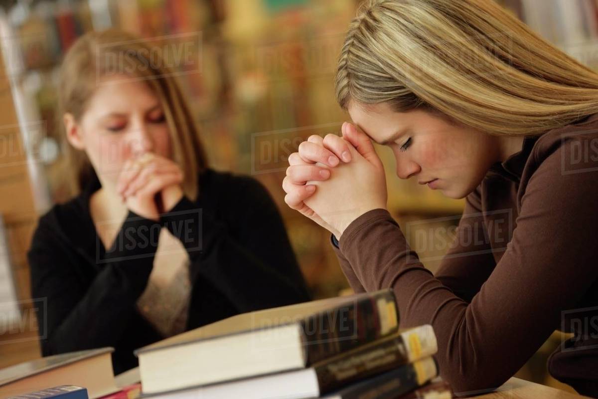 Two Women Praying In Library - Stock Photo - Dissolve