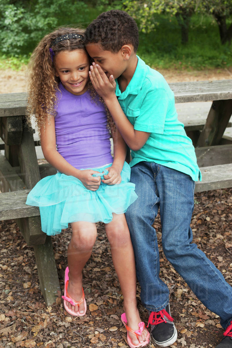 Brother and sister in a park whispering in each other's ears; Menlo ...