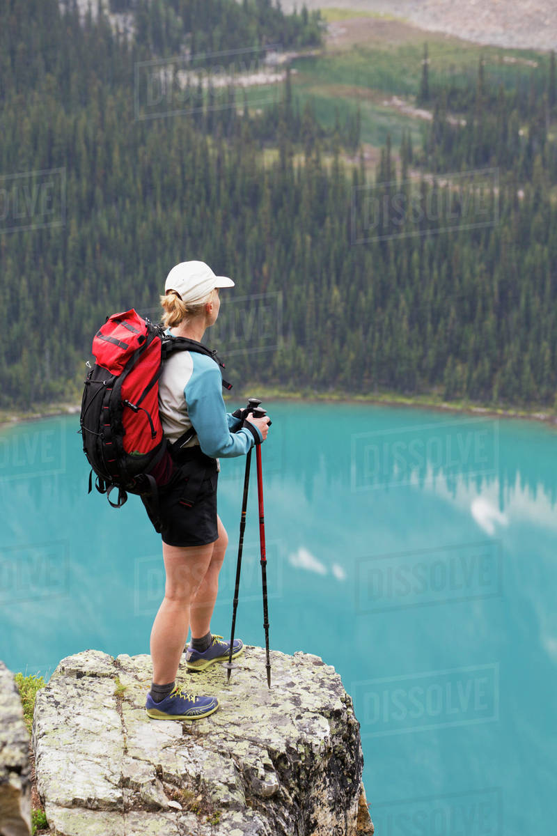 Female hiker on rock cliff overlooking blue alpine lake; British ...