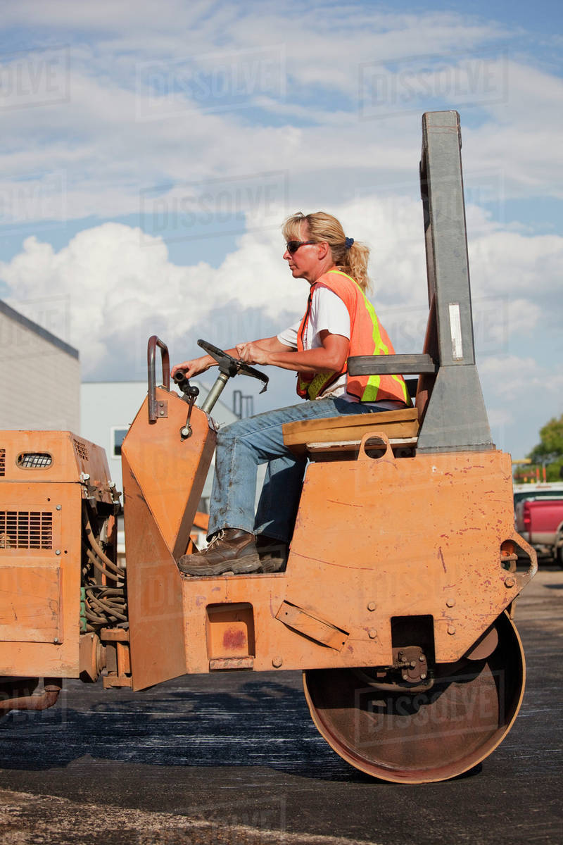 Female operator driving steam roller repairing pot holes in a parking ...