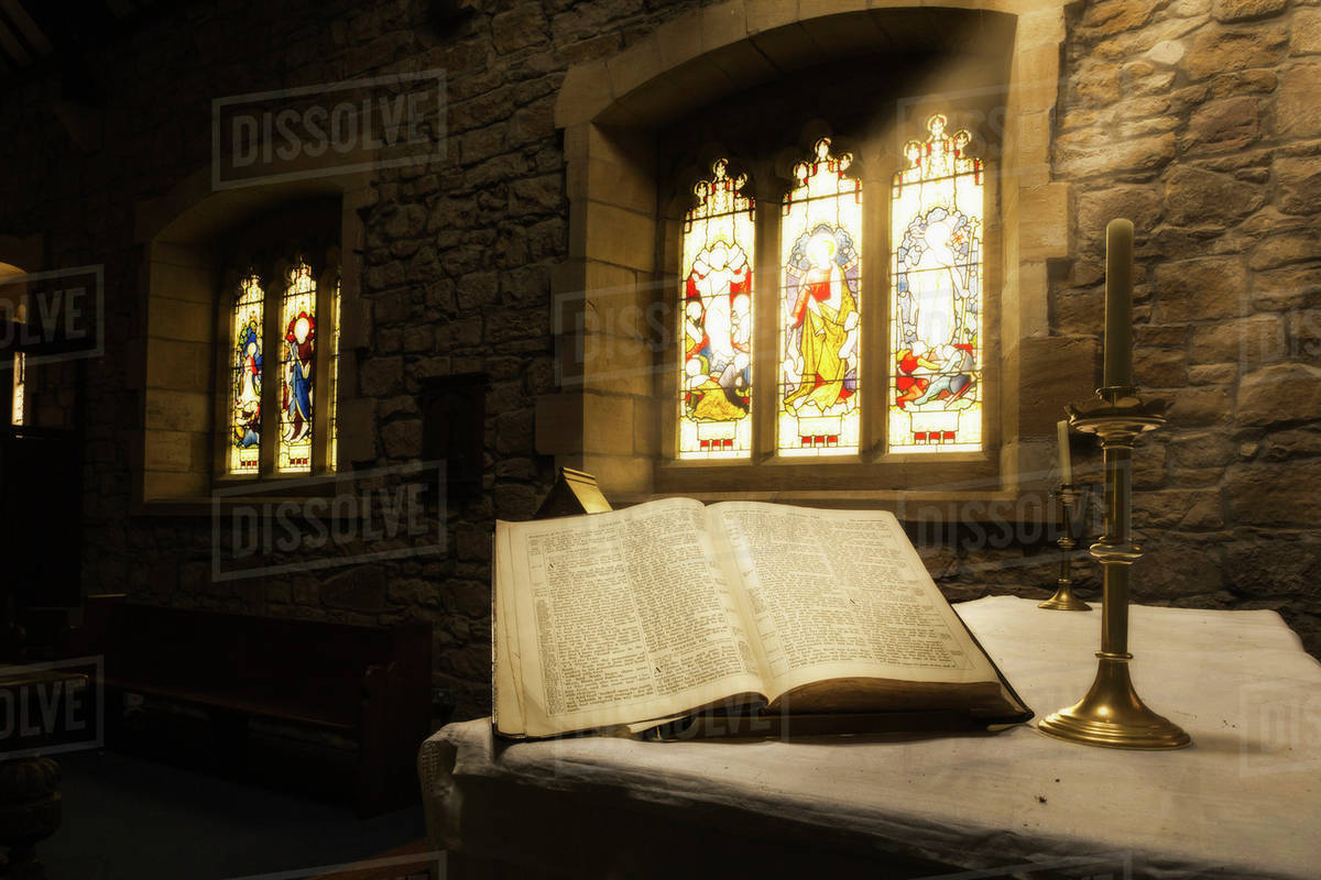 An open Bible on display in a church with colourful stained glass ...