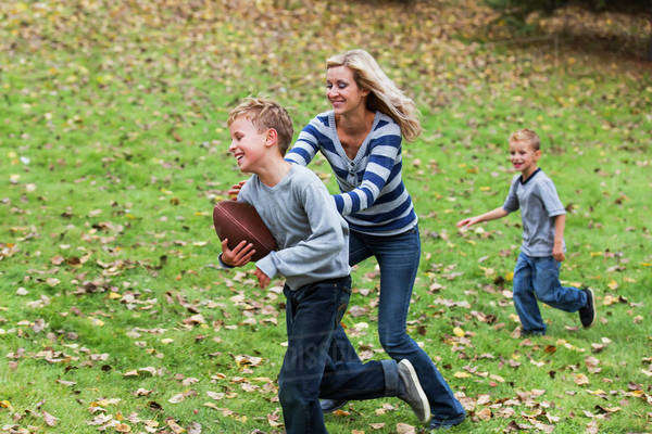 A mother playing football with her sons in a park during autumn ...